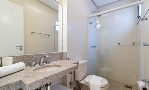 Uma casa de banho com lavatório de mármore, sanita, chuveiro com porta de vidro e um porta-toalhas.