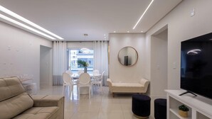 Uma sala de estar moderna com sofá, televisão e área de jantar com cadeiras e mesa.