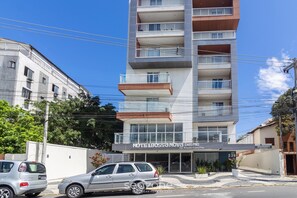 Um hotel de vários andares com varandas, um letreiro com a inscrição 'HOTEL BOSSA NOVA' e um estacionamento com carros.