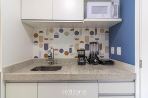 Cozinha com micro-ondas, cafeteira e liquidificador sobre a bancada.