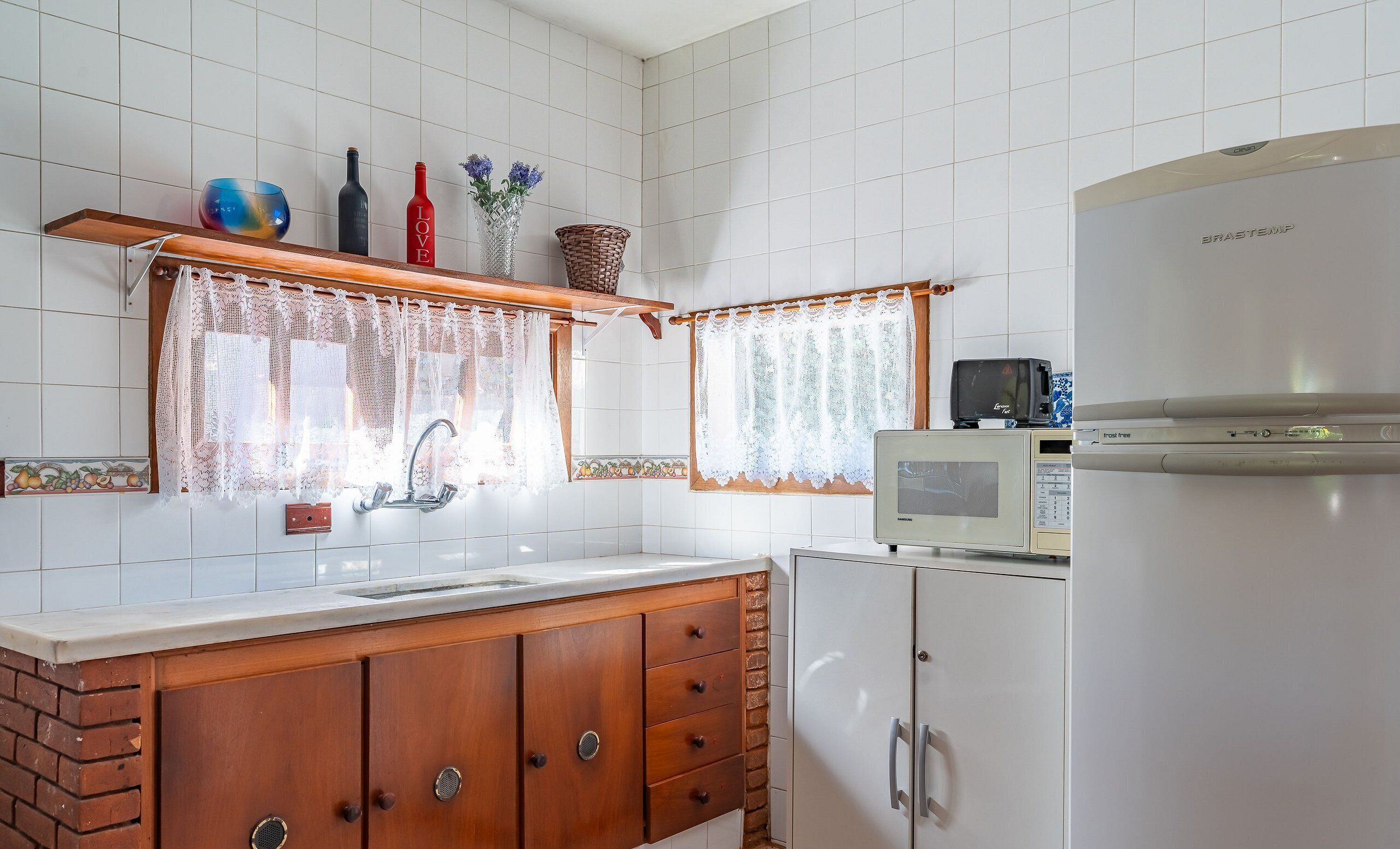 Uma cozinha com azulejos brancos, um armário de madeira, um micro-ondas e uma geladeira.