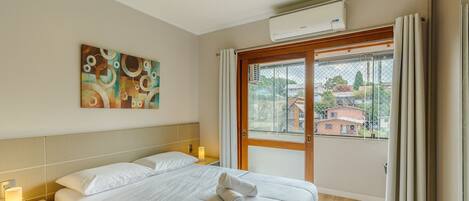 Quarto de hotel com cama, um quadro na parede e janela com vista para edifícios.