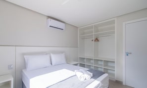 Quarto de hotel moderno com cama bem arrumada, guarda-roupa embutido e ar condicionado fixado na parede.