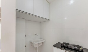 Casa de banho com azulejos brancos, lavatório branco e bancada preta com um objeto preto em cima.