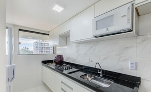 Uma cozinha moderna com armários brancos, bancada preta, micro-ondas embutido e janela com vista para um edifício.
