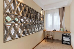 Um quarto com parede estampada em padrão geométrico, uma escrivaninha com cadeira, uma janela com cortinas e um radiador.