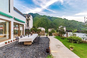 Um restaurante com mesas ao ar livre, ao fundo montanhas e um rio.