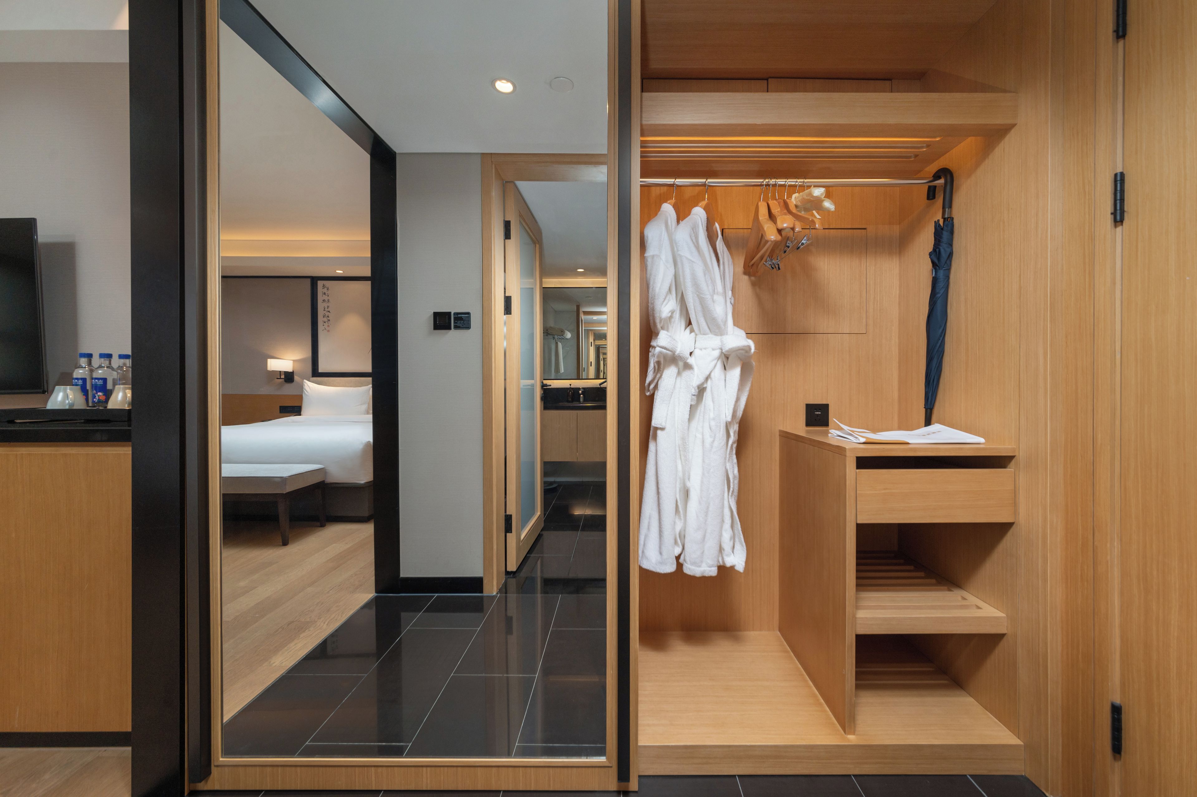 Quarto de hotel com cama, mesa de cabeceira e espelho. Armário de madeira com roupão pendurado na porta.