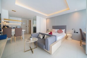 Quarto de hotel moderno com cama, sofá, mesa de jantar e cozinha compacta.