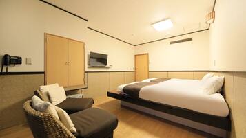 Quarto de hotel com cama, televisão, guarda-roupa, telefone e uma pequena área de estar.