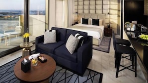 Quarto de hotel moderno com cama, sofá, área de refeições e vista para a cidade.