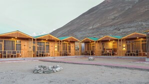 Uma fileira de cabanas de madeira com grandes janelas e telhado plano, com montanhas ao fundo.