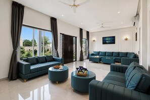 Uma sala de estar ampla com um amplo sofá, uma mesa de centro e vista para um jardim através de grandes janelas.