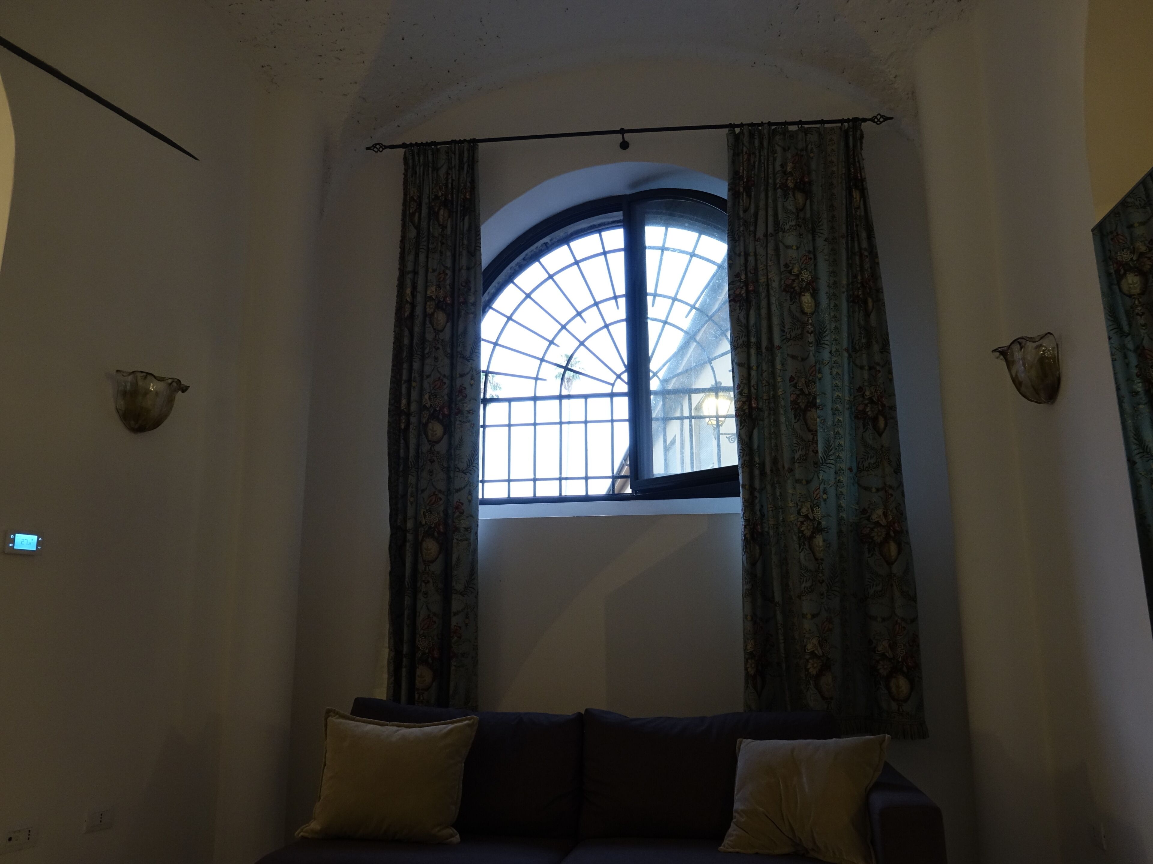 Um quarto com teto arredondado, janela com padrão de grade e sofá com almofadas.