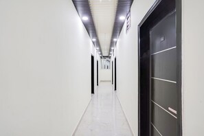 Corredor com piso branco, porta preta à direita e teto com iluminação embutida.