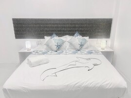 Uma cama com cobertura branca, duas mesas de cabeceira com abajures e uma cabeceira com design texturizado.