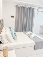 Quarto de hotel com cama, mesa de cabeceira, abajur, janela com cortinas e ar condicionado.
