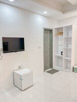 Um banheiro moderno com pia branca, espelho, televisão fixada na parede e um closet espaçoso com prateleiras e cabideiro.
