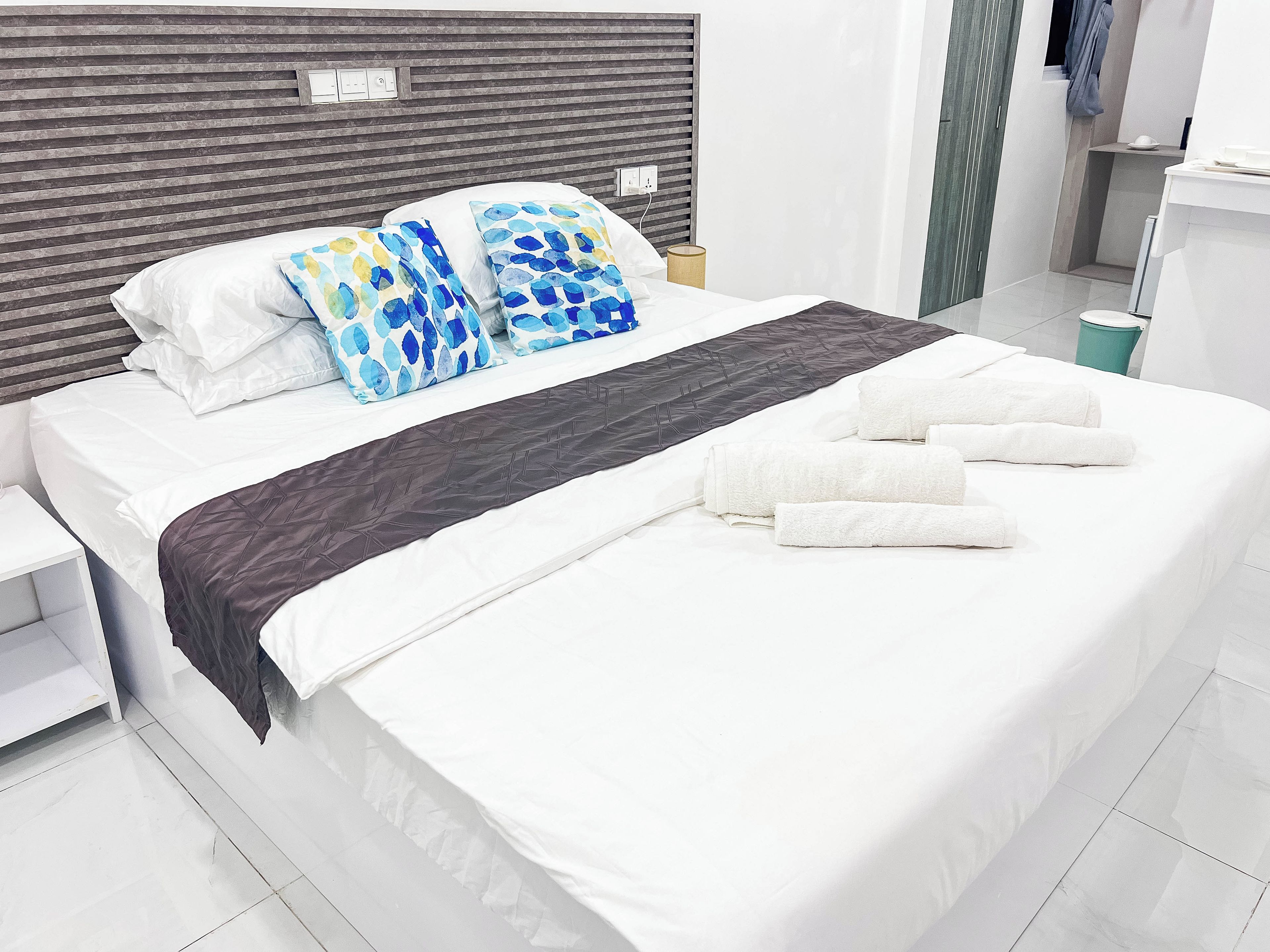 Cama bem arrumada com lençóis brancos, cabeceira escura e travesseiro com padrão azul e branco.