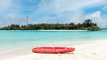 Uma praia com um caiaque vermelho na areia, águas turquesa cristalinas e uma ilha arborizada ao fundo.