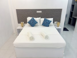 Cama bem arrumada com duas almofadas e duas toalhas enroladas, mesa de cabeceira com abajur e cabeceira com painel de controle.