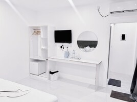 Quarto de hotel moderno com escrivaninha branca, televisão de tela plana, espelho redondo e armário embutido.