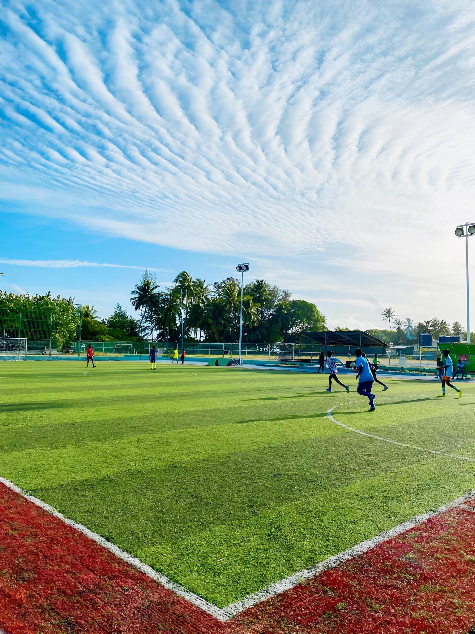 Um campo de futebol com jogadores, traves e um céu limpo.