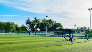 Um campo de futebol com jogadores, traves e um céu limpo.