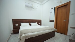 Quarto com cama de madeira, roupa de cama branca, piso de mármore, porta de madeira e ar condicionado.