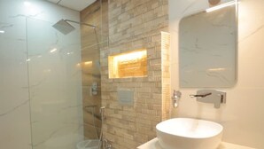 Um banheiro moderno com chuveiro em box de vidro, vaso sanitário branco e toucador com bancada de mármore.