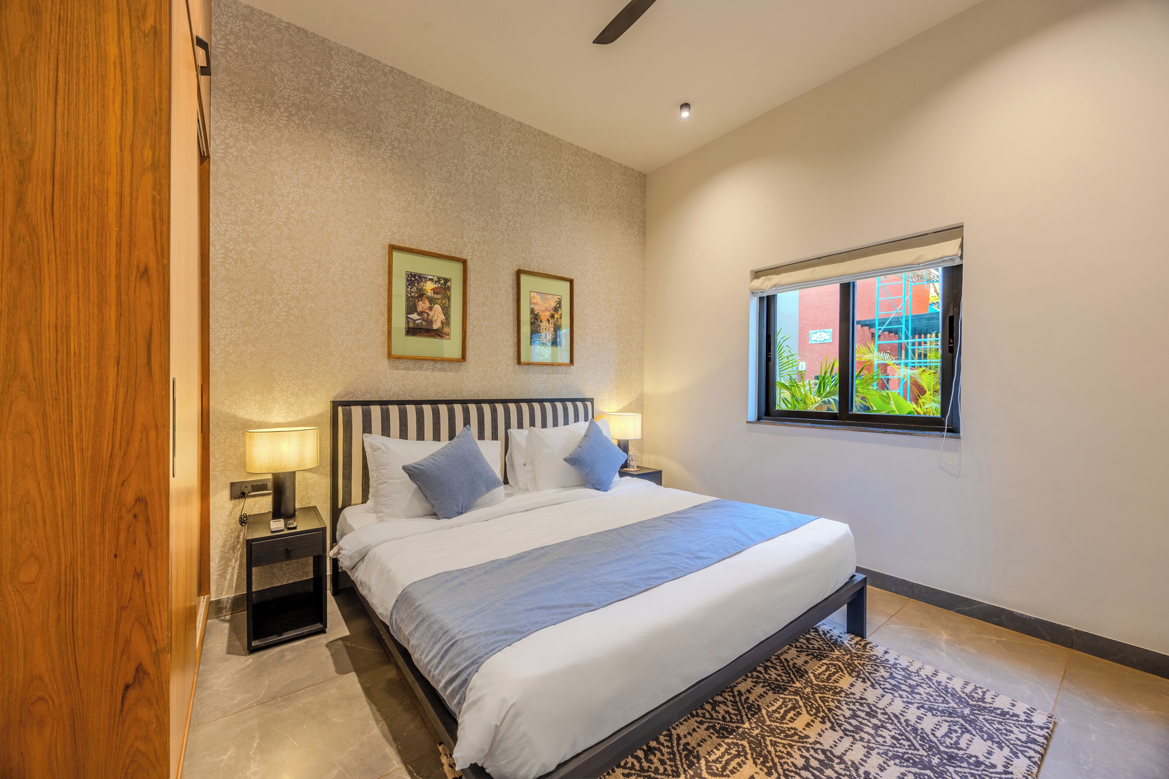 Quarto de hotel com cama, mesas de cabeceira, janela com vista e duas imagens emolduradas na parede.