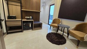Uma sala de estar moderna com um sofá, uma mesinha e uma televisão. Há uma estante de madeira e um alto-falante preto no chão.