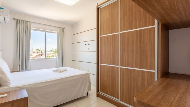 Quarto de hotel com uma cama, guarda-roupa de madeira, secretária e janela com cortinas.