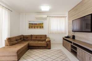 Uma sala de estar com sofá seccional, televisão de tela plana, armário de madeira e tapete estampado.