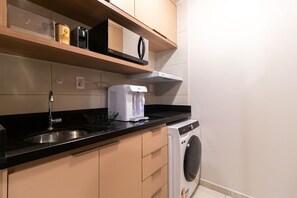 Uma cozinha compacta com máquina de lavar, cafeteira e micro-ondas na bancada.