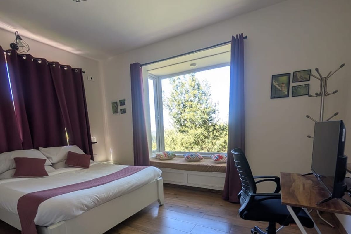 Quarto com cama, escrivaninha e cadeira, janela com cortinas e luminária pendente.