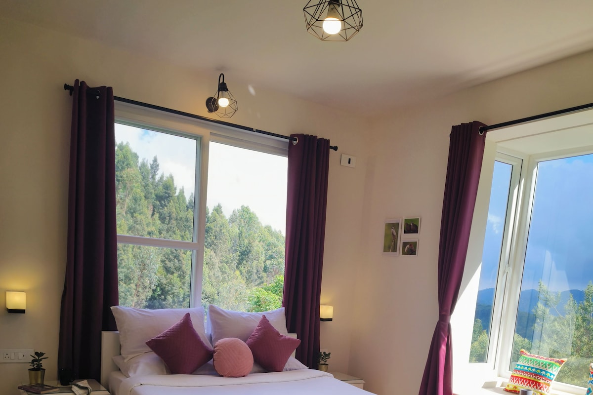 Quarto com cama, mesas de cabeceira, janela com cortinas e vista para árvores, além de um tapete tecido.