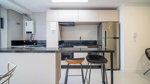 Uma cozinha moderna com fogão embutido, geladeira e aquecedor de água. Há dois bancos e uma cadeira.