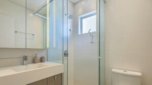 Uma casa de banho moderna com cabine de duche em vidro, sanita e lavatório com espelho em cima.