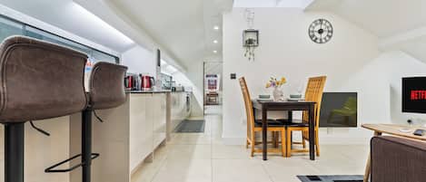 Uma cozinha moderna com área de refeições, televisão e relógio na parede.