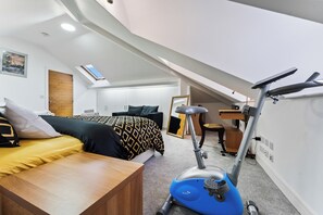 Quarto compacto com cama, escrivaninha e bicicleta ergométrica.