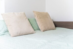 Cama com cobertura acolchoada e dois travesseiros, um listrado e outro liso.