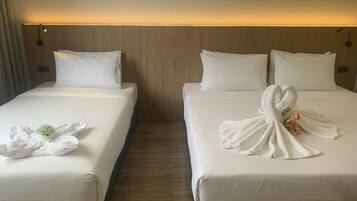 Duas camas de hotel com lençóis brancos, uma cabeceira de madeira e uma luminária fixada na parede.