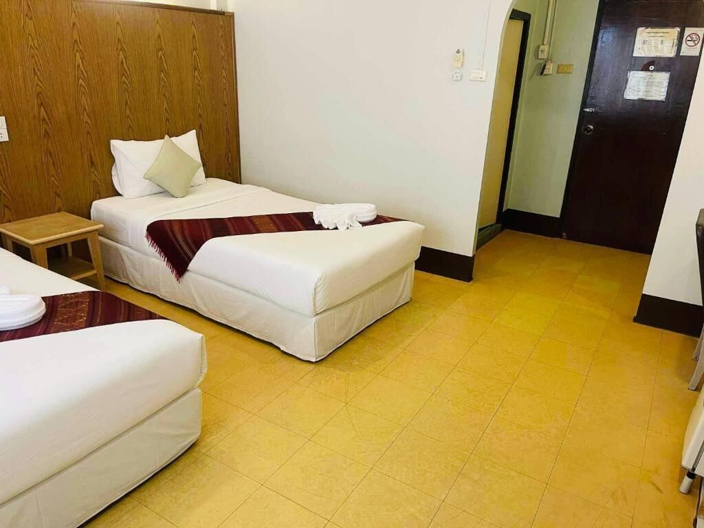 Quarto de hotel com duas camas de solteiro, cabeceira de madeira, mesa de cabeceira pequena e piso ladrilhado.
