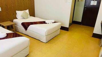 Quarto de hotel com duas camas de solteiro, cabeceira de madeira, mesa de cabeceira pequena e piso ladrilhado.