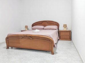 Quarto com cama de madeira, duas mesas de cabeceira e um criado-mudo.
