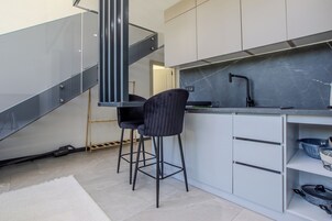 Cozinha moderna com painel de fundo de mármore, uma cadeira preta e uma escada.