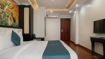 Quarto de hotel com cama, televisão, escrivaninha e porta.