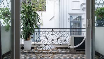 Uma varanda com planta em vaso, guarda-corpo de metal decorativo e piso de azulejos.