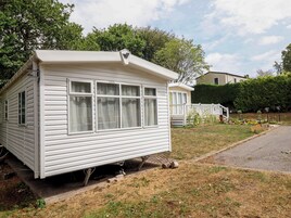 Uma casa móvel com varanda frontal, um pequeno deck e um jardim com vasos de plantas.